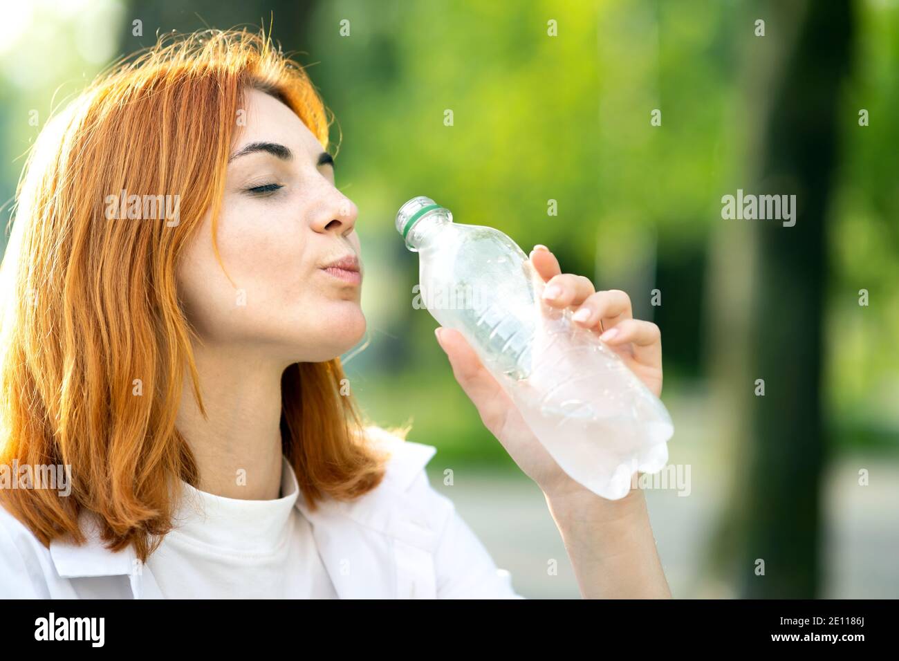 Happy thirsty redhead woman drinking fresh bottled water in summer ...