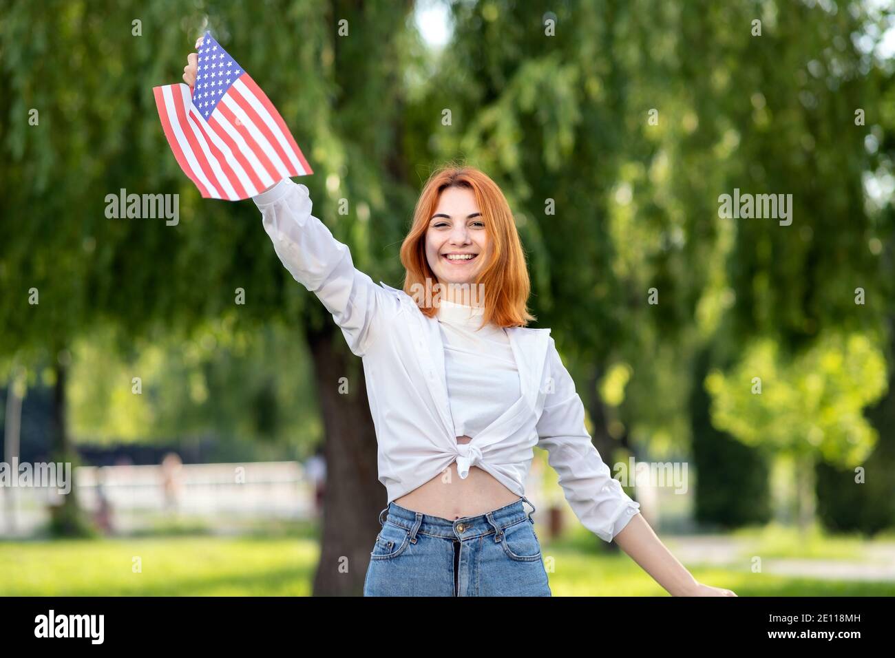 Angry young red haired woman protester posing with USA national flag in ...