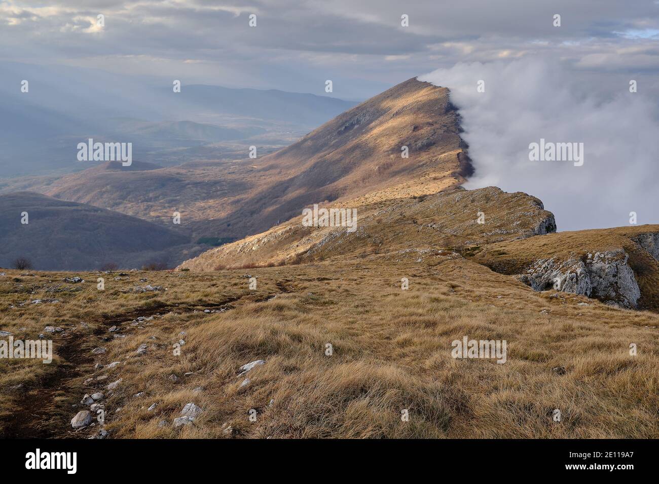 Golden, dry grass and distant mountain ridge covered by thick mist and ...
