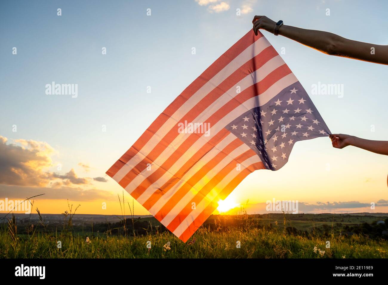 Human hands holding waving american national flag in field at sunset ...
