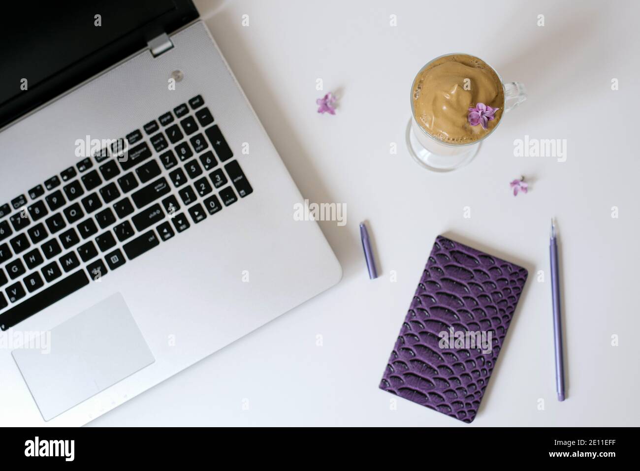 Dalgona coffee in a clear mug, Notepad, pen and computer on the table ...