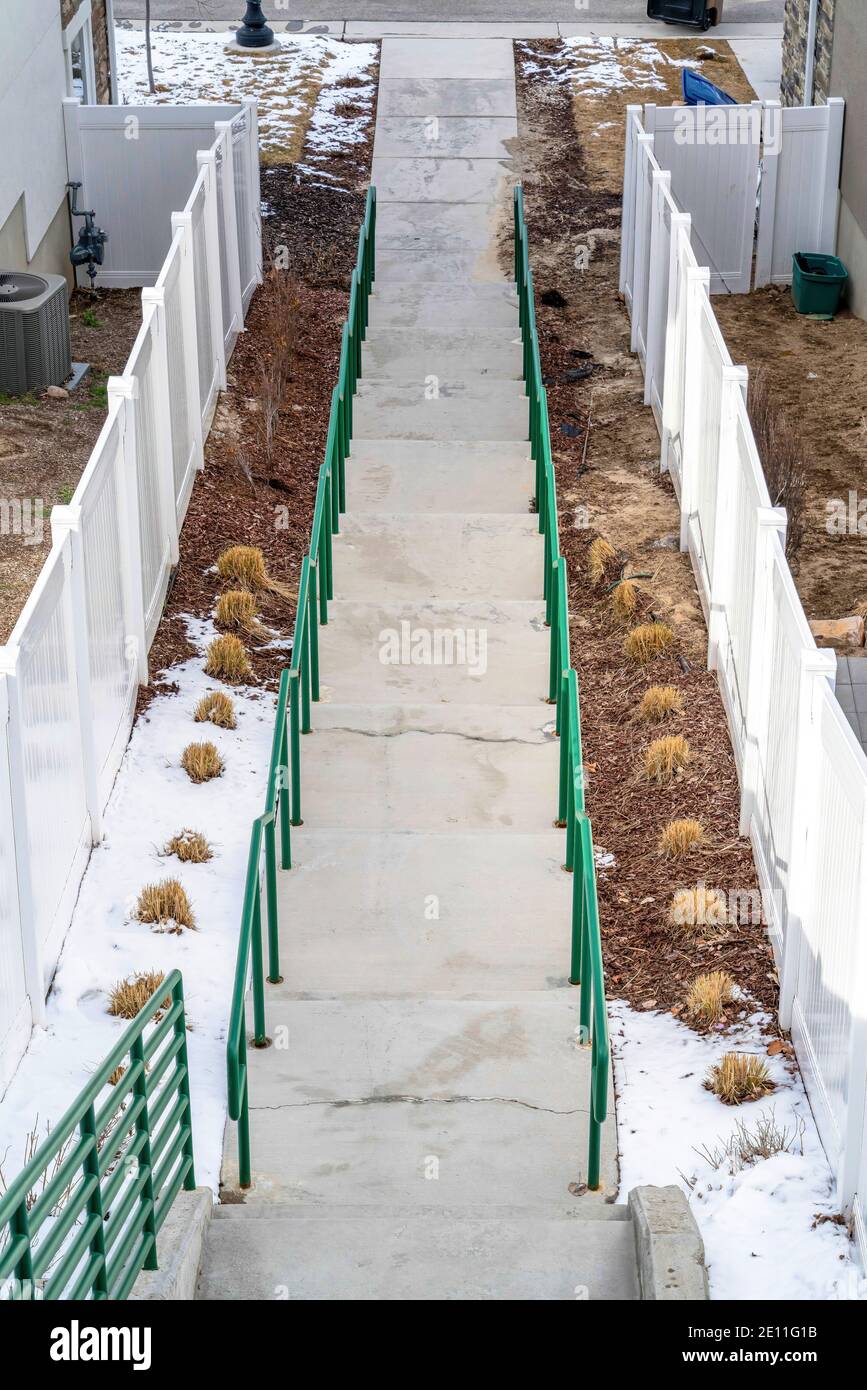 Concrete stairs with green handrails amid snowy yards and white wooden ...