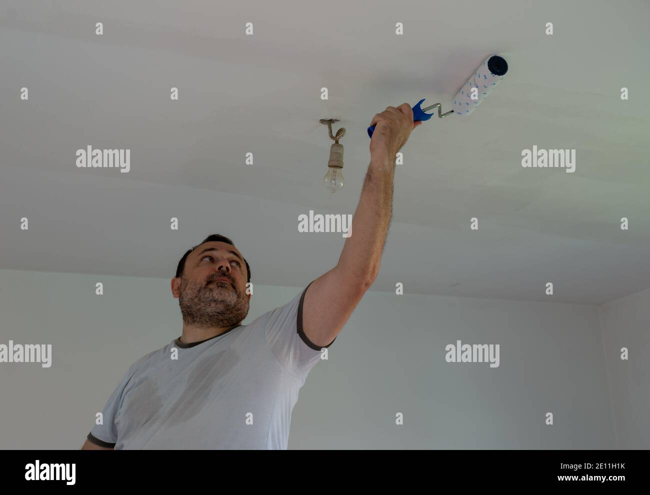 Hard working man painting ceiling with a roller in white Stock Photo ...
