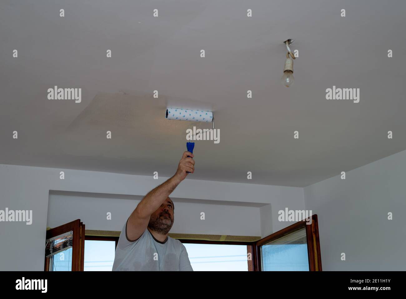 Hard working man painting ceiling with a roller in white Stock Photo ...