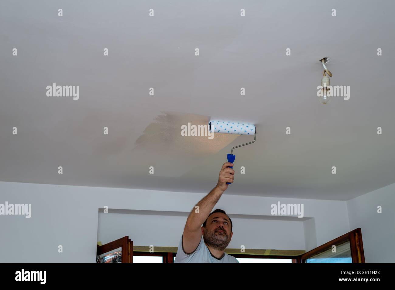 Hard working man painting ceiling with a roller in white Stock Photo ...