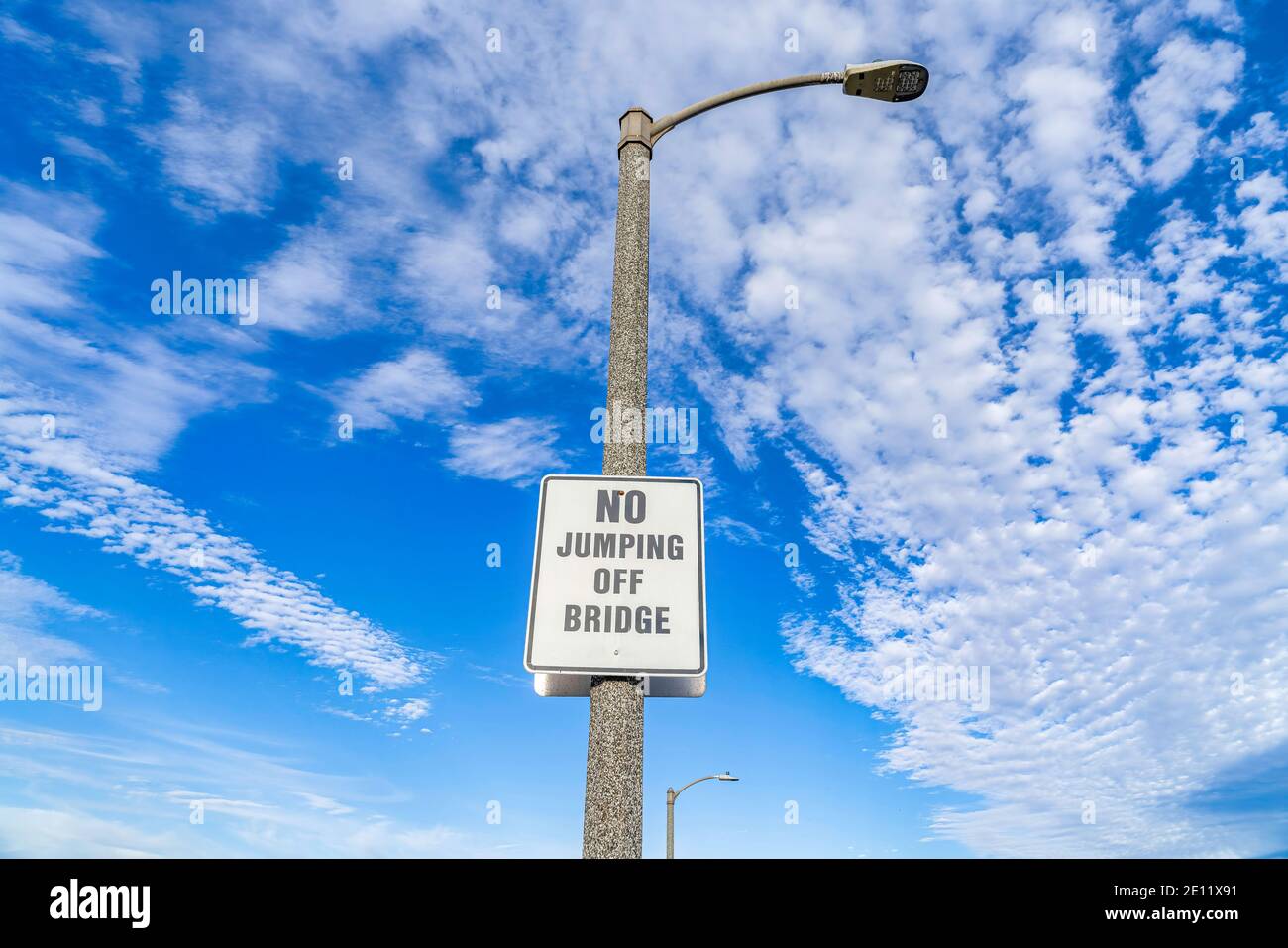 No Jumping Off Bridge sign on lamp post against blue sky and puffy ...