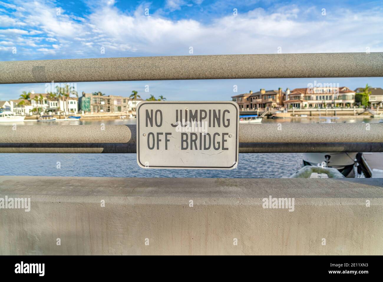 No Jumping Off Bridge sign with sea waterfront houses and cloudy sky ...