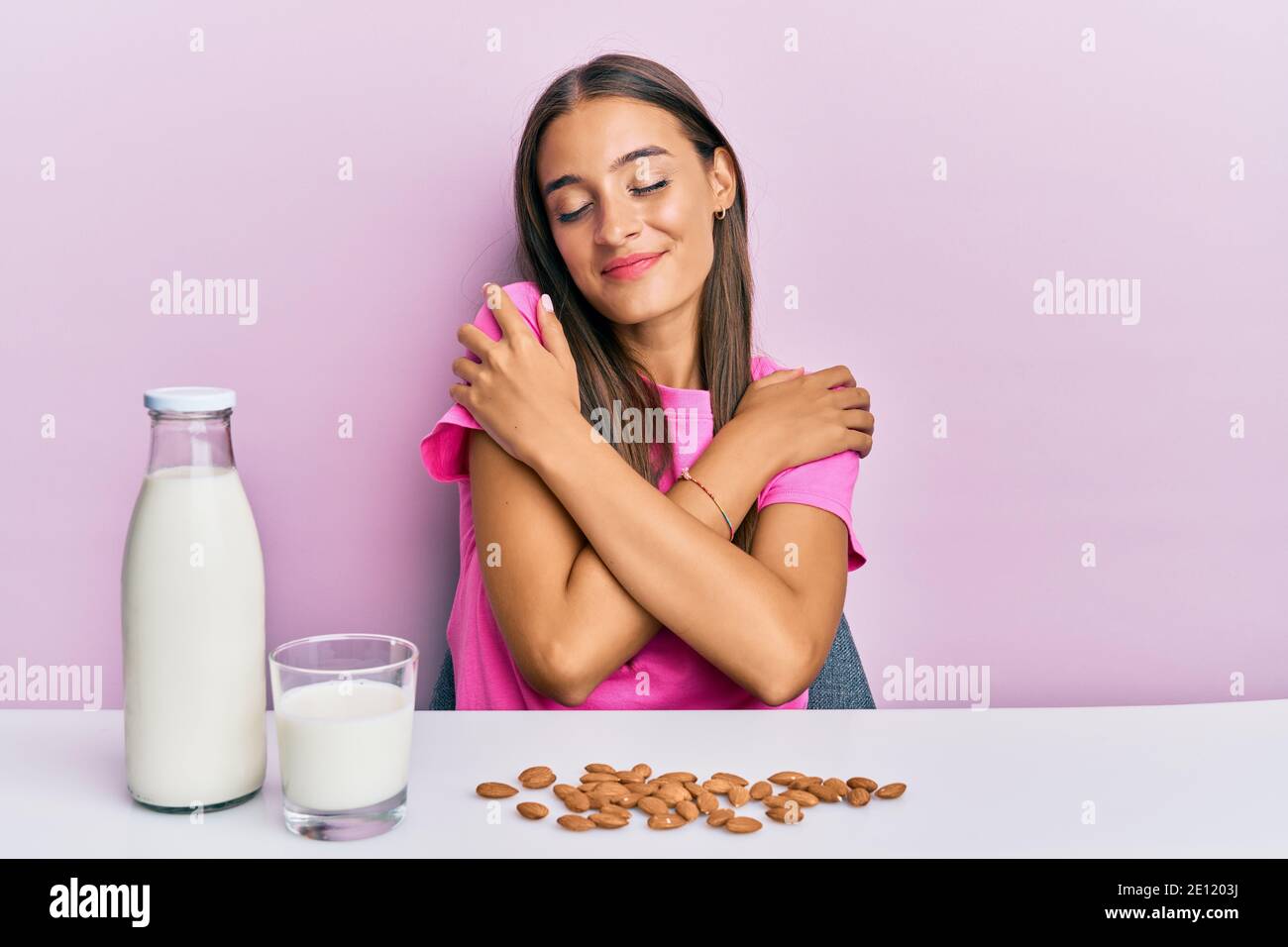 Young hispanic woman drinking healthy almond milk sitting on the table ...