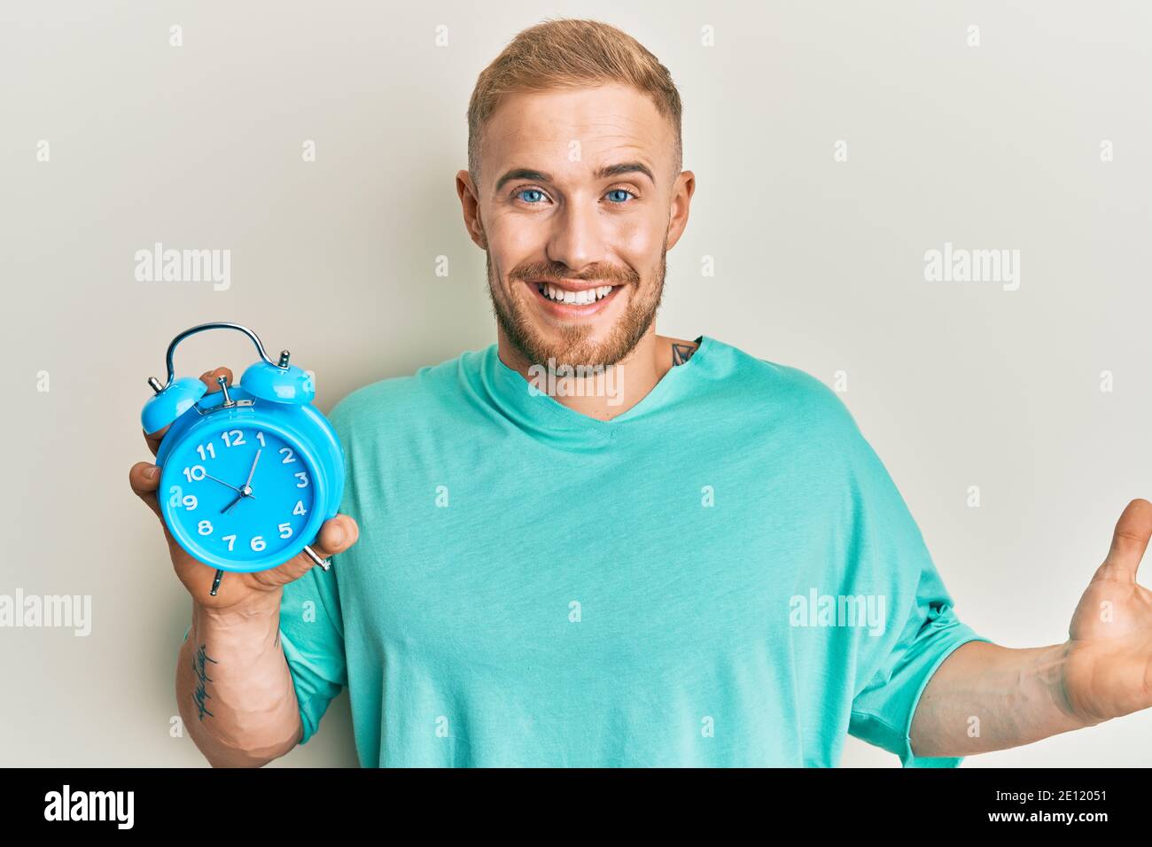 Young caucasian man holding alarm clock celebrating achievement with ...