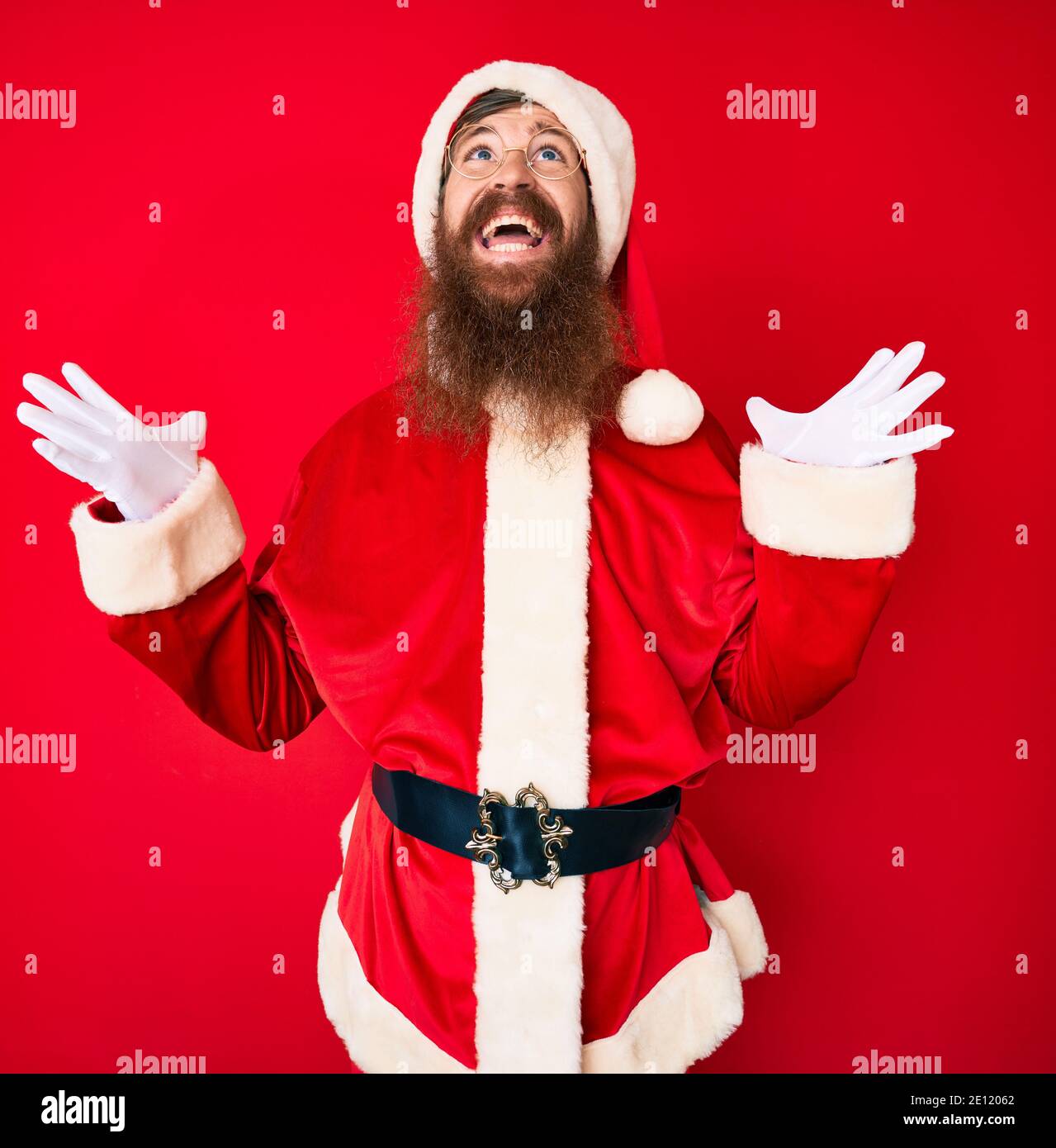 Handsome young red head man with long beard wearing santa claus costume ...