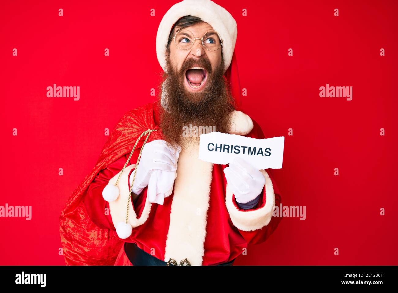 Handsome young red head man with long beard wearing santa claus costume ...