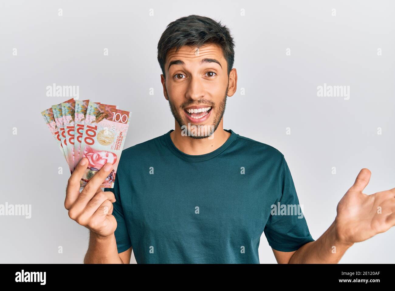 Young handsome man holding 100 new zealand dollars banknote celebrating ...