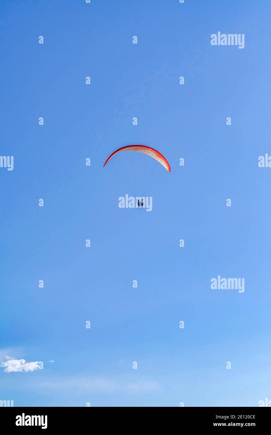 Parachuter with red parachute flying against blue sky in San Diego ...