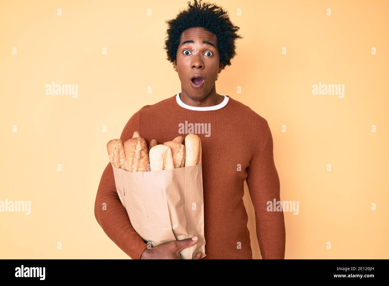 Handsome african american man with afro hair holding paper bag with ...