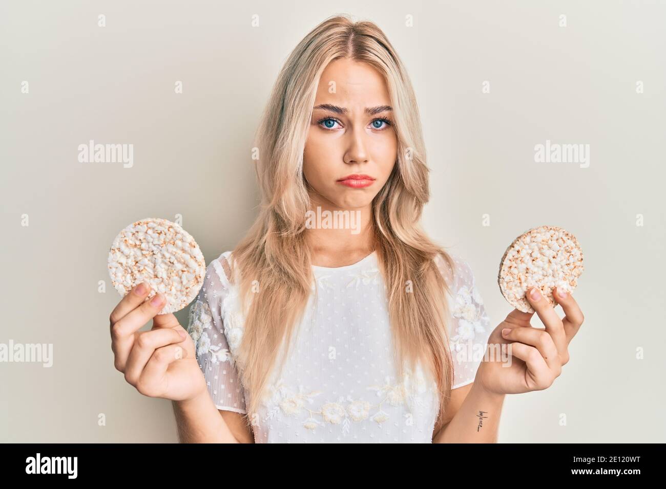 Beautiful caucasian blonde girl eating healthy rice crackers depressed ...