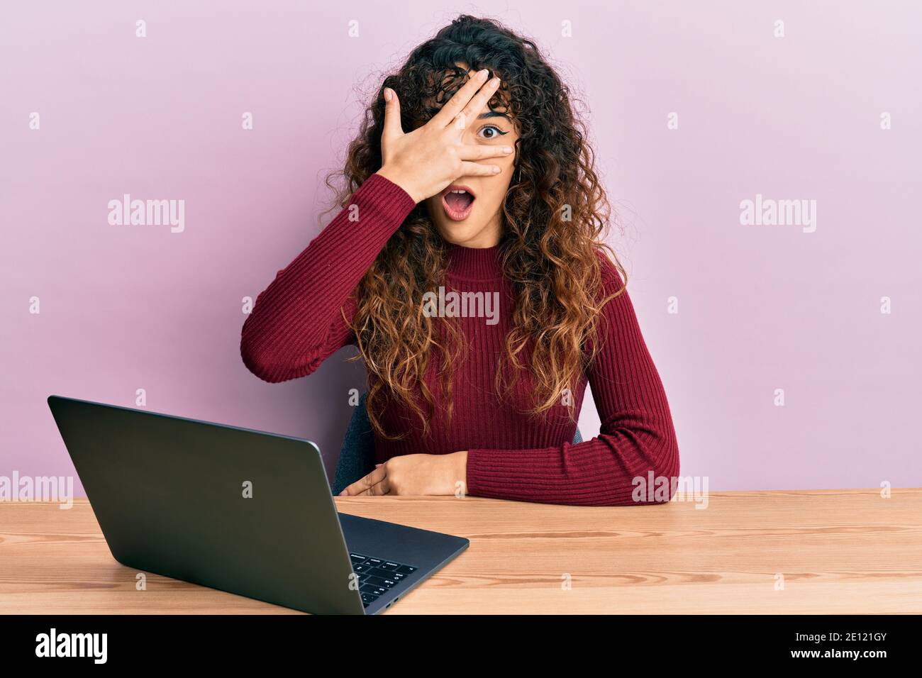 Young hispanic girl working using computer laptop peeking in shock ...