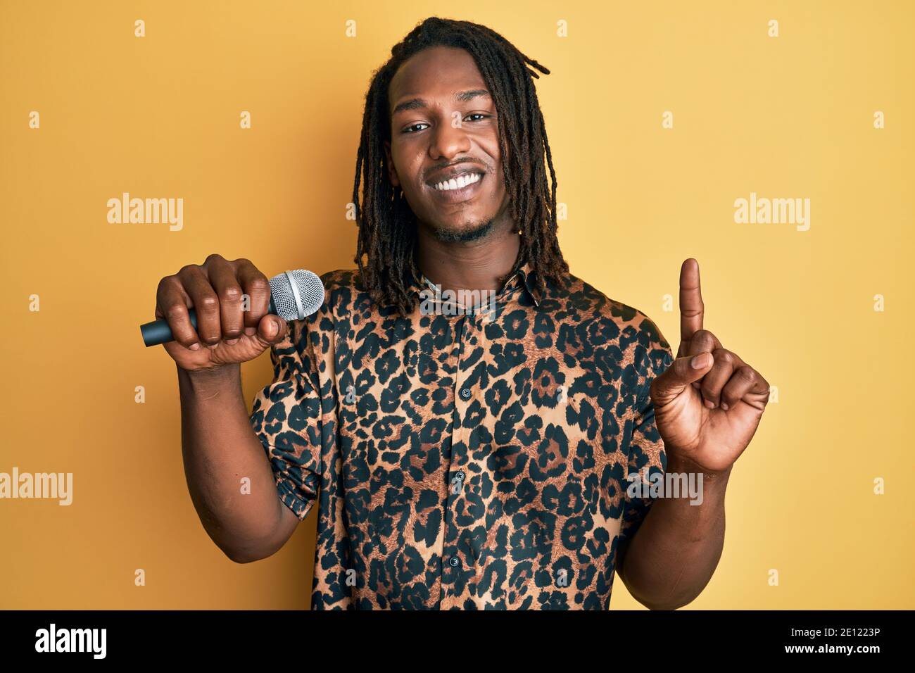 African american man with braids singing song using microphone smiling ...