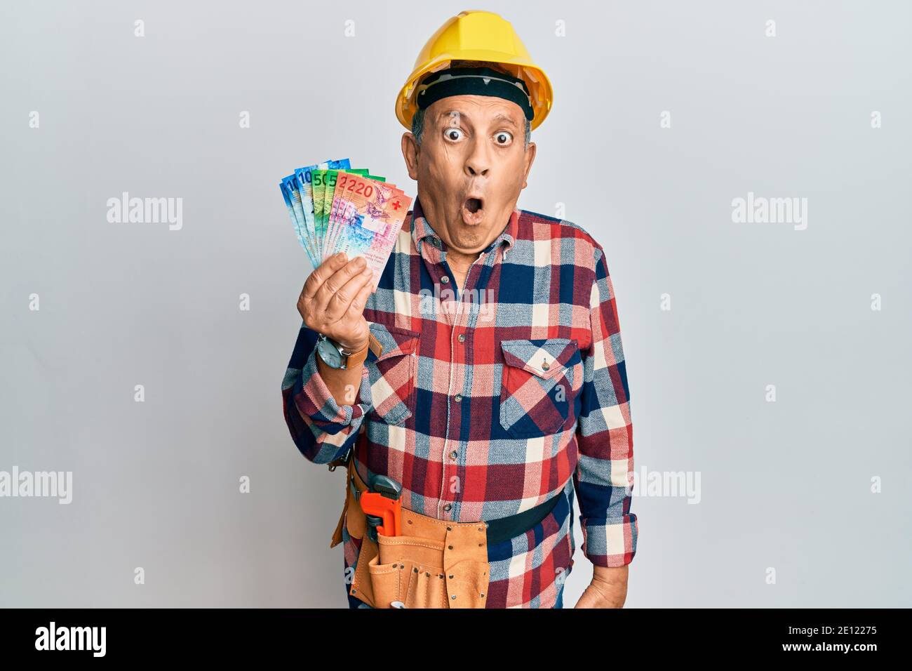 Senior hispanic man wearing handyman uniform and hardhat scared and ...