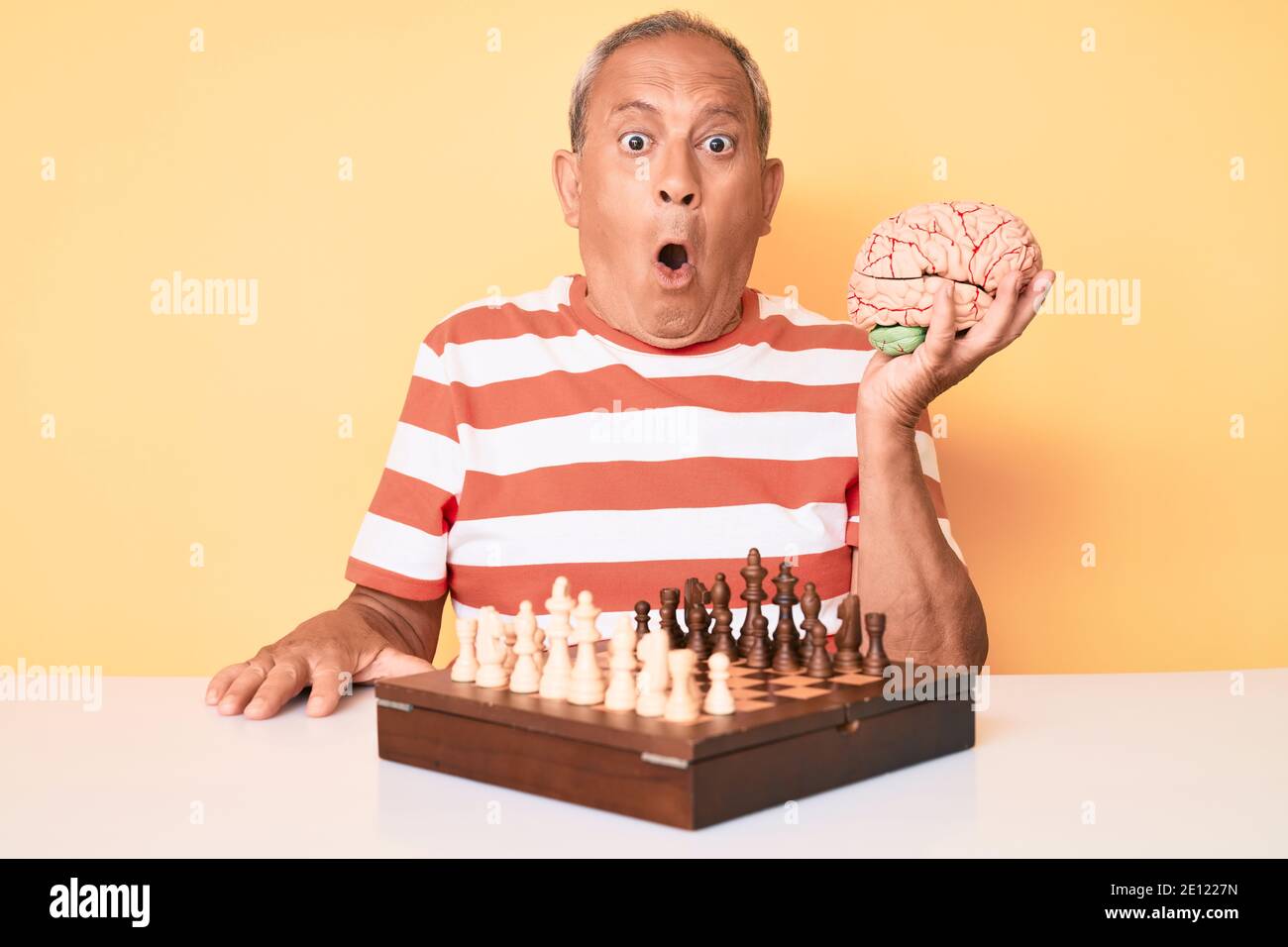 Senior handsome man with gray hair holding brain while playing chess ...