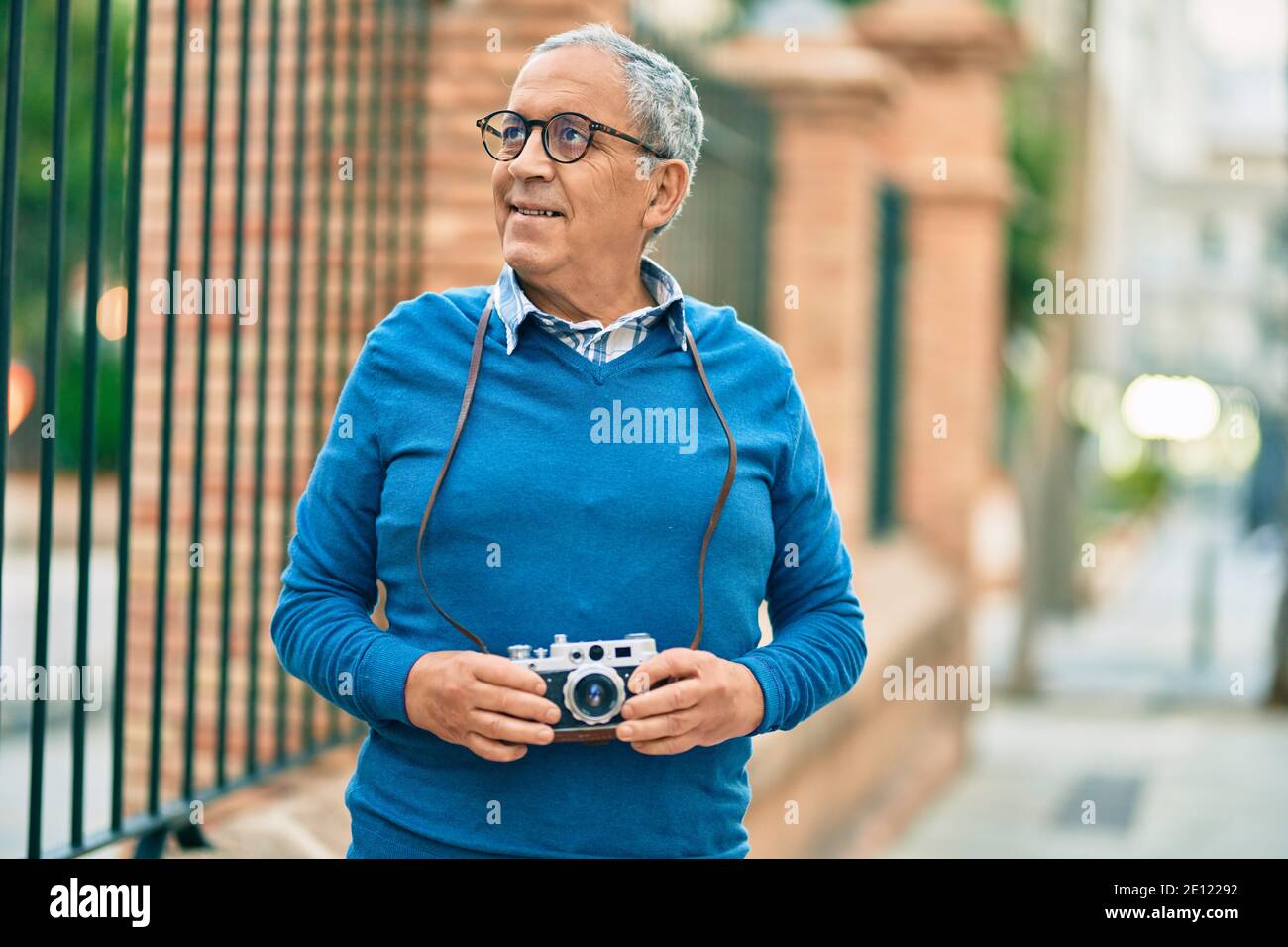 Senior grey-haired tourist man smiling happy using vintage camera at ...