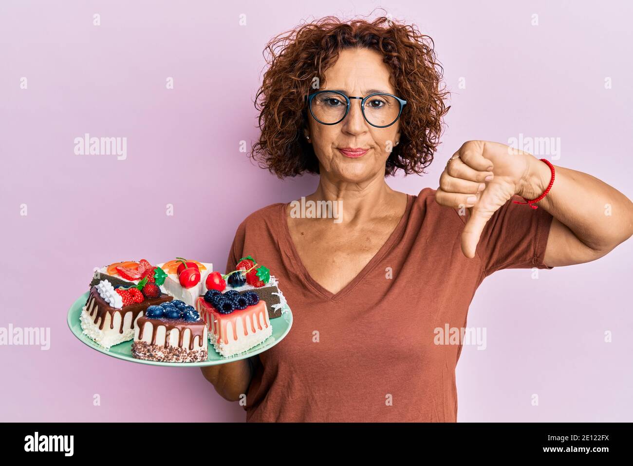 Beautiful middle age mature woman holding cake slices with angry face ...