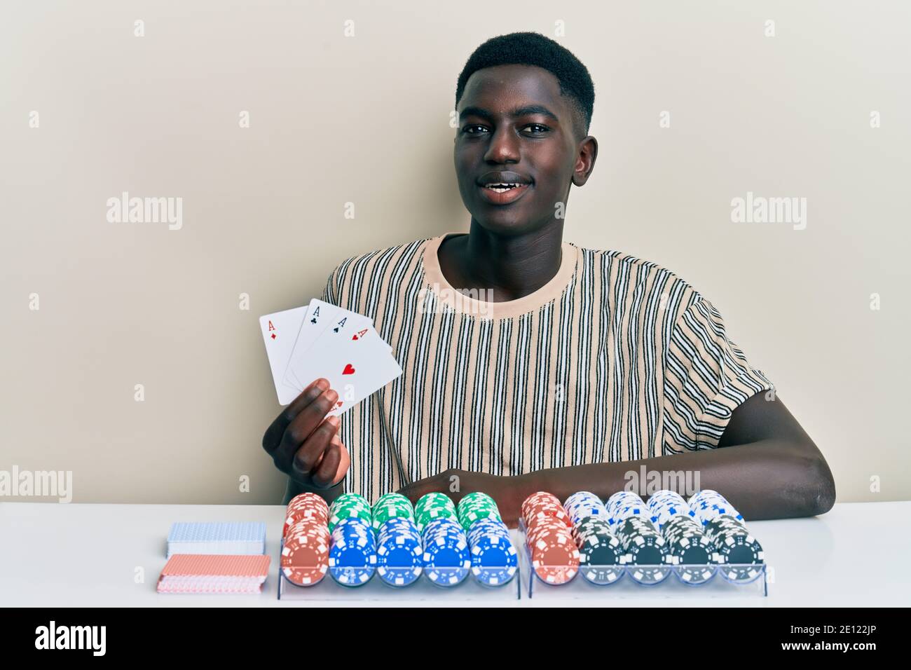 Young african american man playing poker holding cards looking positive ...