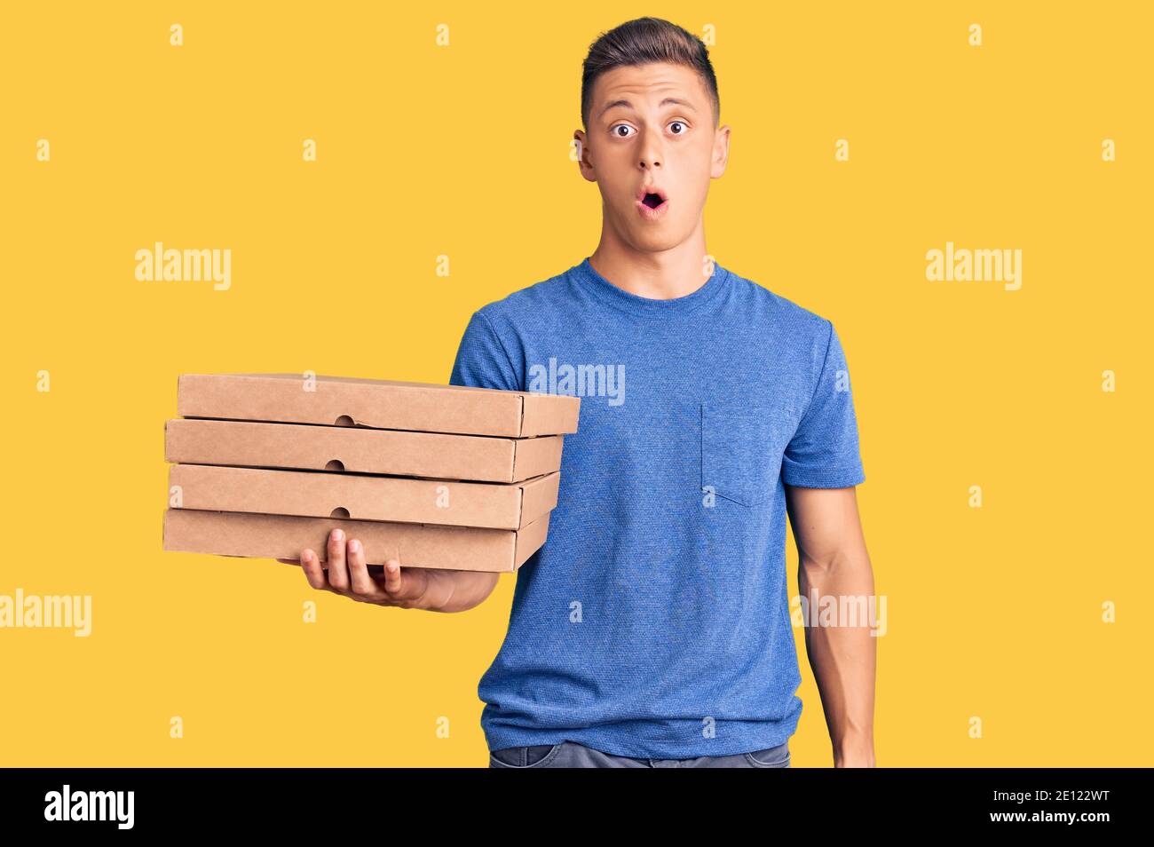 Young handsome hispanic man holding delivery pizza box scared and ...