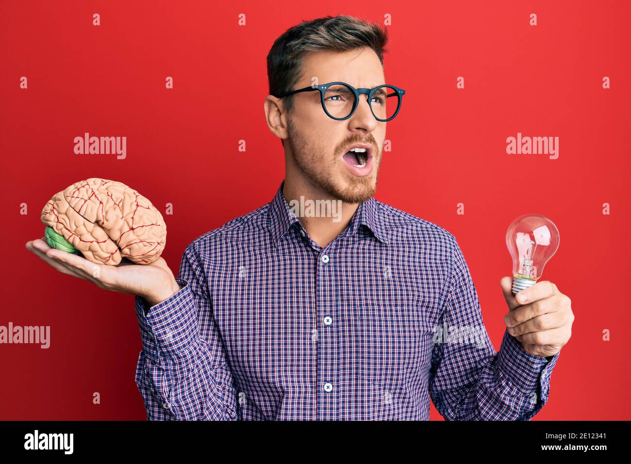 Handsome caucasian man holding brain and lightbulb for inspiration and ...