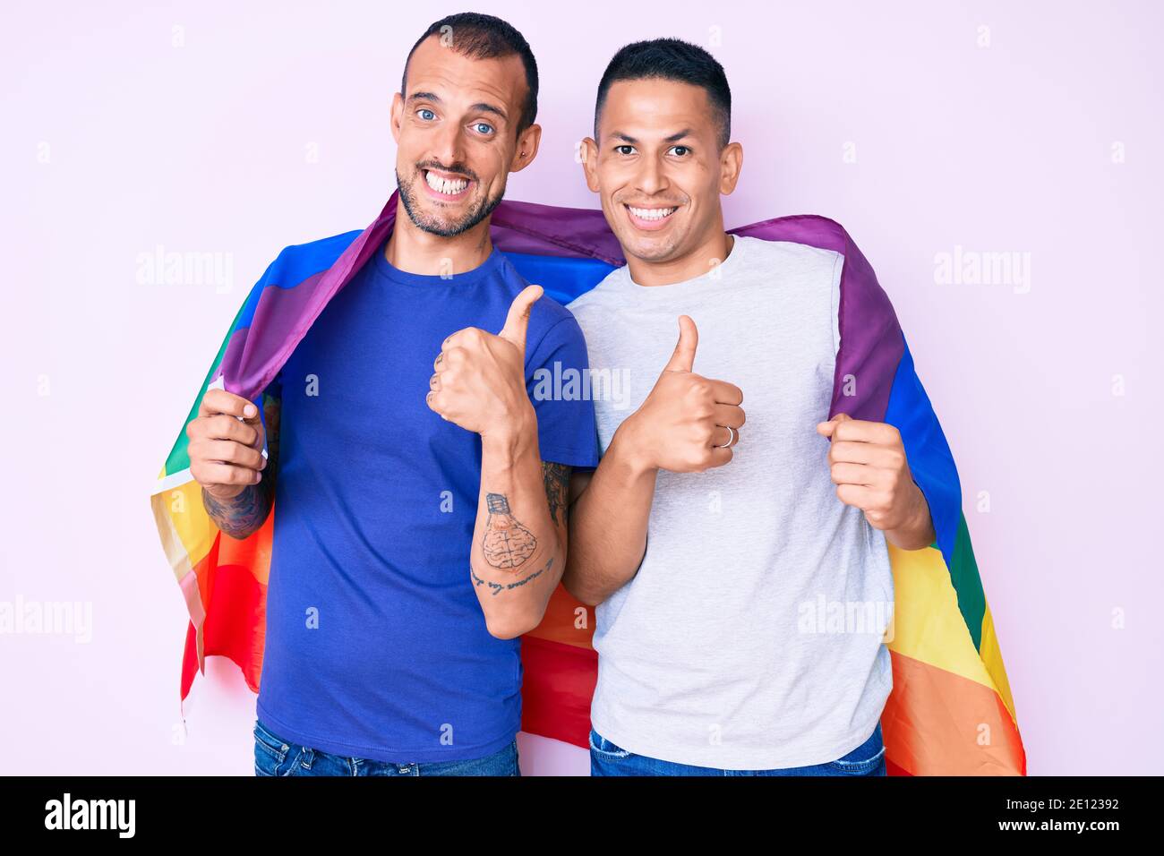 Young gay couple of two men holding rainbow lgbtq flag together smiling ...