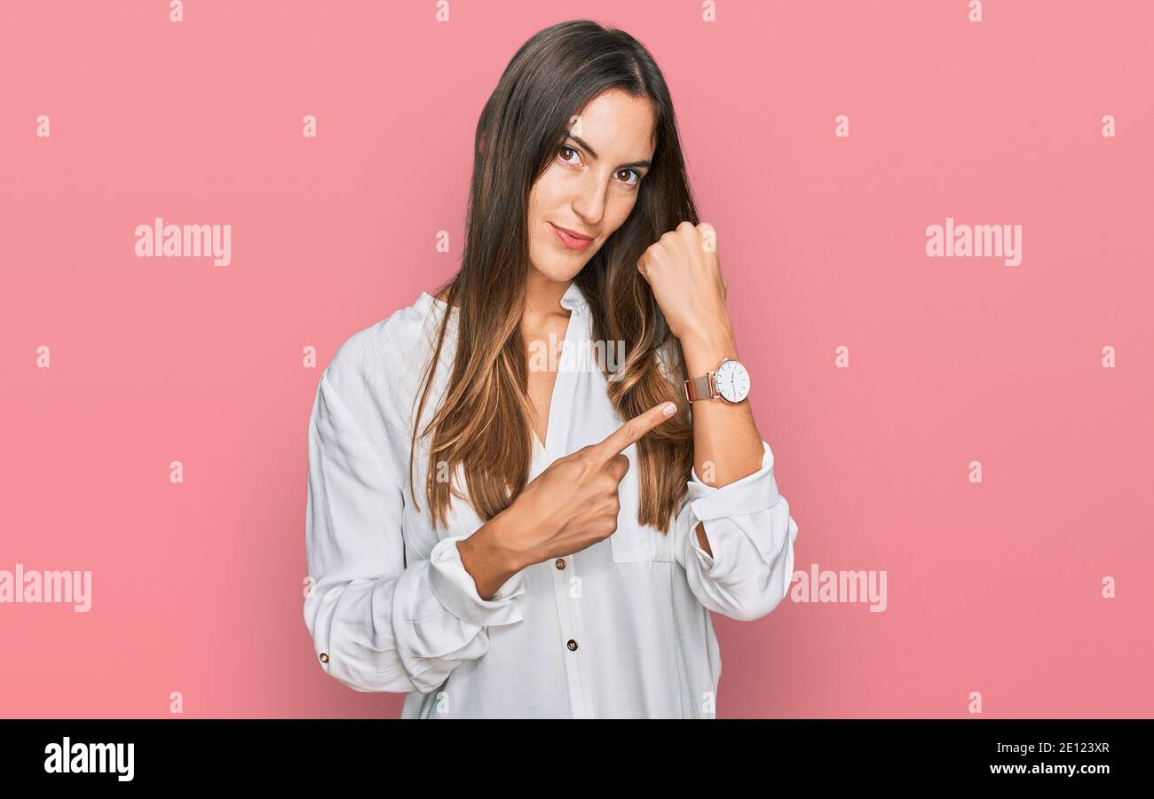 Young beautiful woman wearing casual clothes in hurry pointing to watch ...