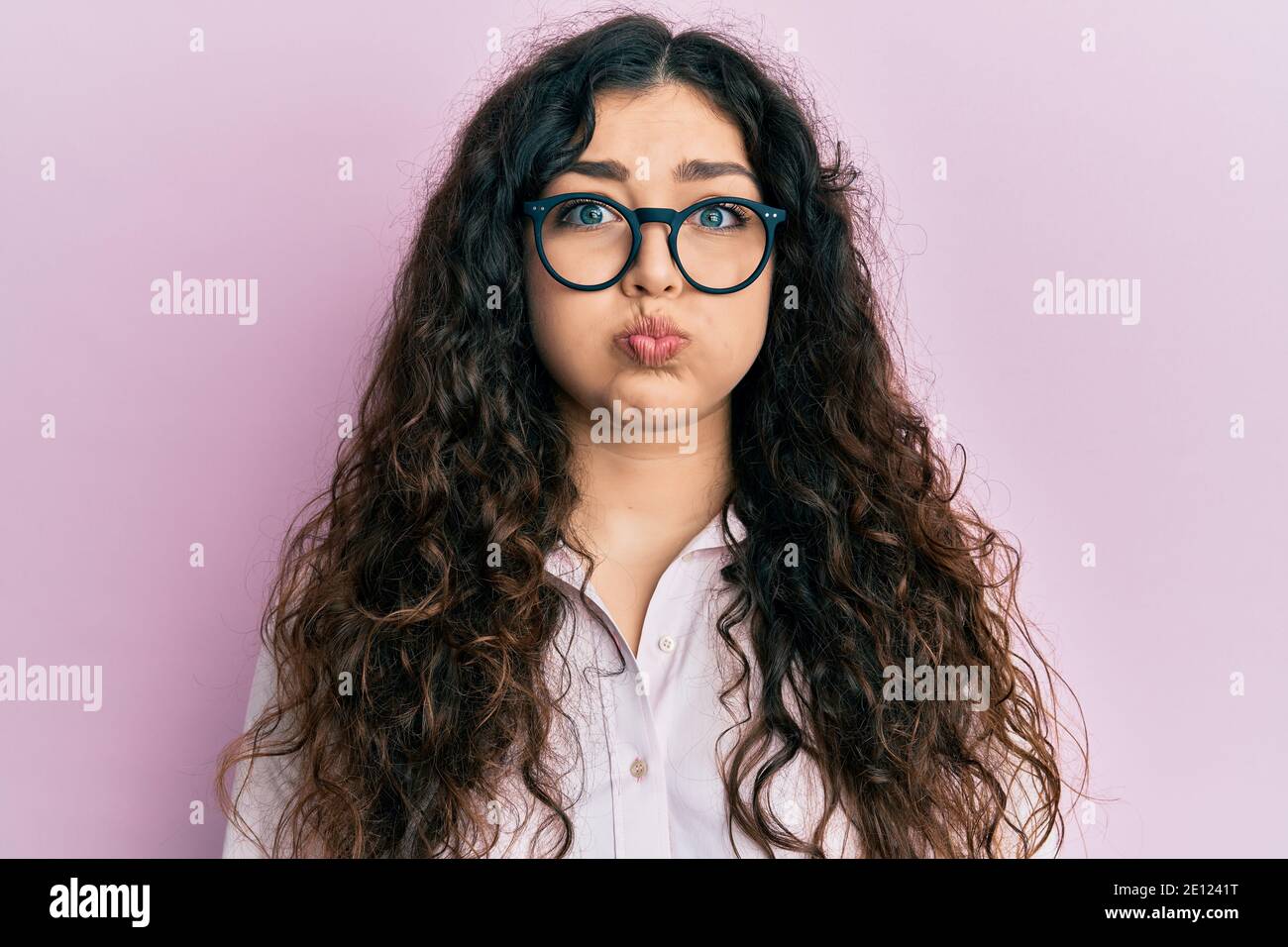 Young brunette woman with curly hair wearing casual clothes and glasses ...