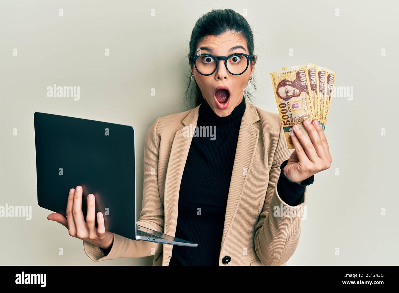 Young hispanic woman wearing business style holding laptop and ...