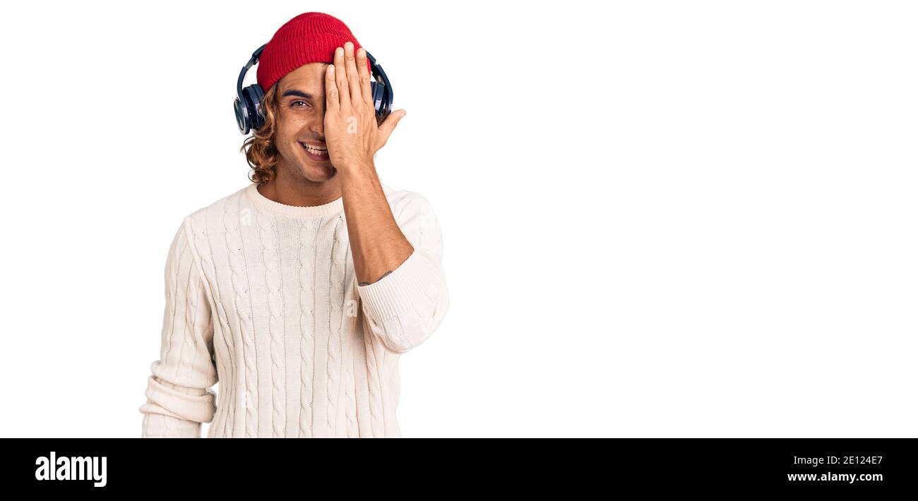 Young hispanic man listening to music using headphones covering one eye ...
