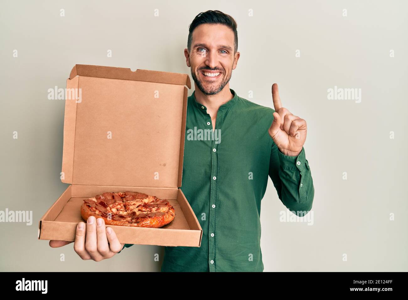 Handsome man with beard holding italian pizza smiling with an idea or ...