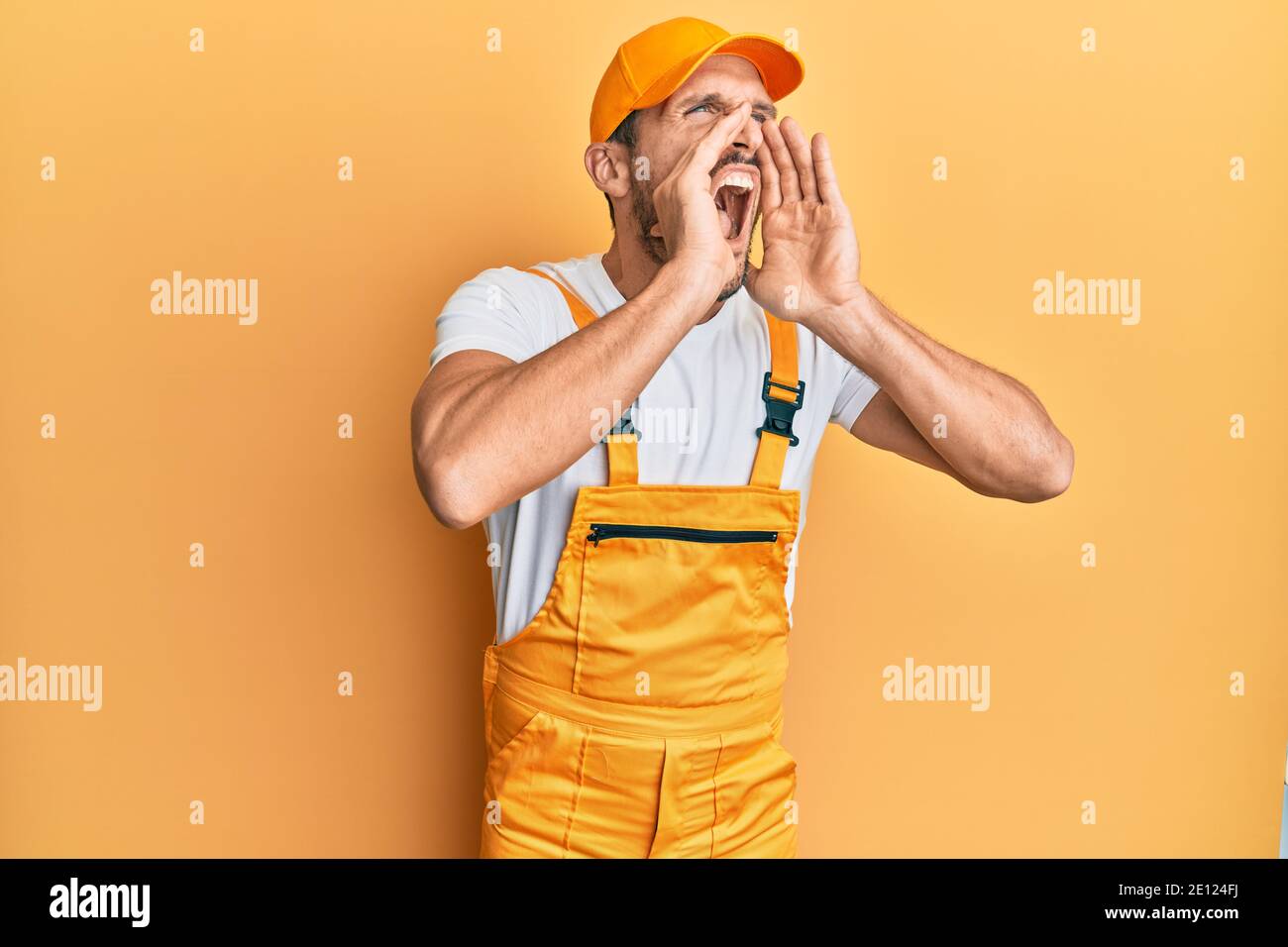 Young handsome man wearing handyman uniform over yellow background ...