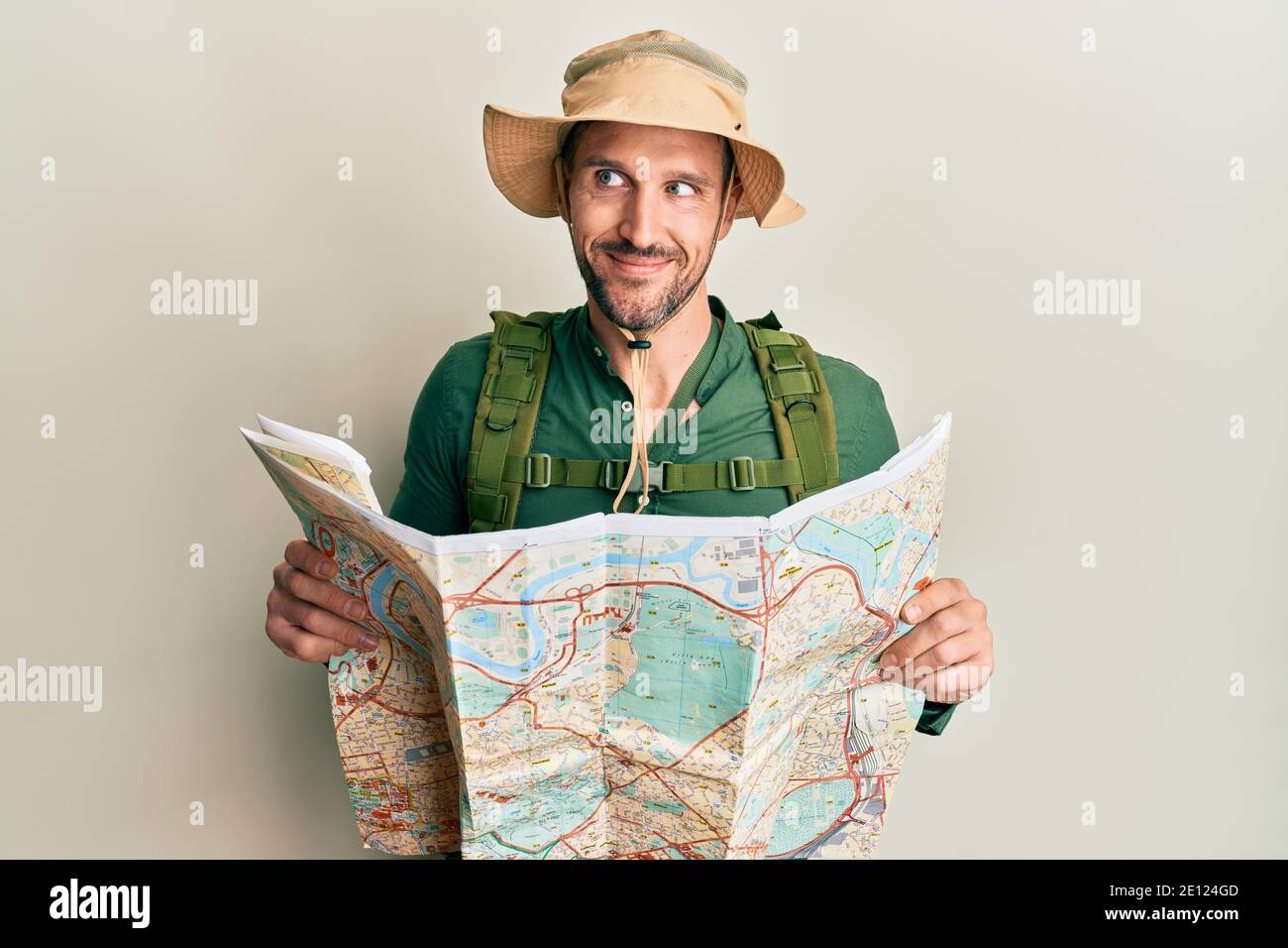 Handsome man with beard wearing explorer hat holding map smiling ...