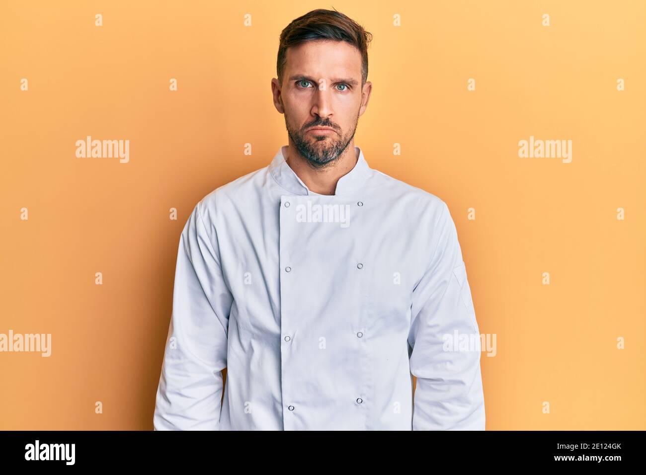 Handsome man with beard wearing professional cook uniform depressed and ...