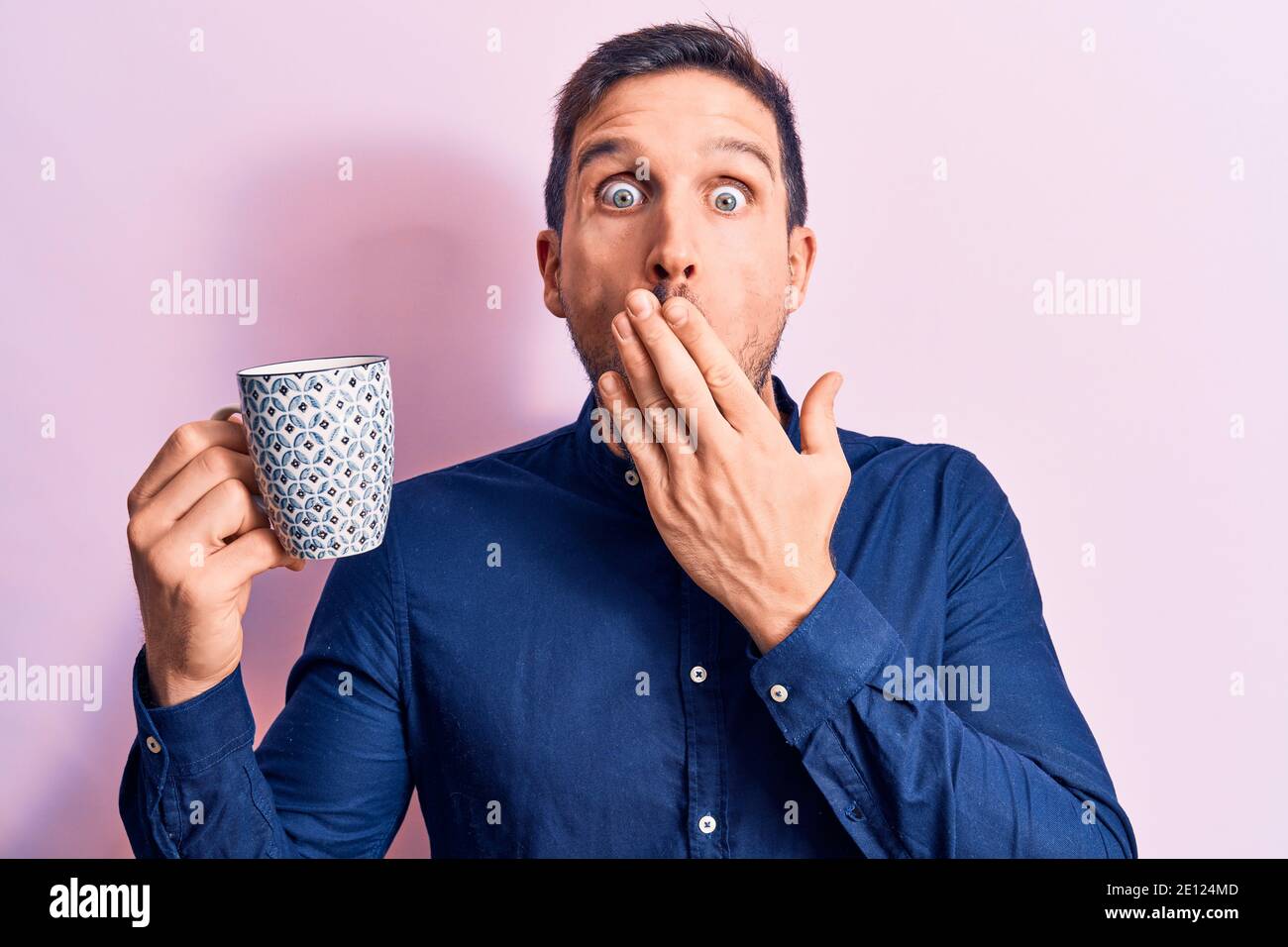 Young handsome businessman drinking mug of coffee over isolated pink ...