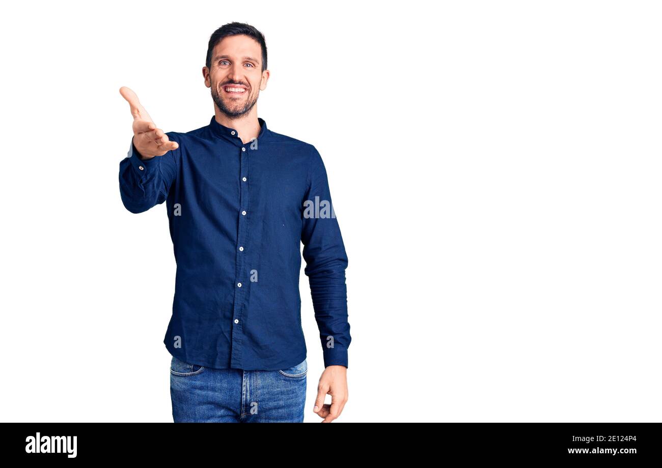 Young handsome man wearing casual shirt smiling friendly offering ...
