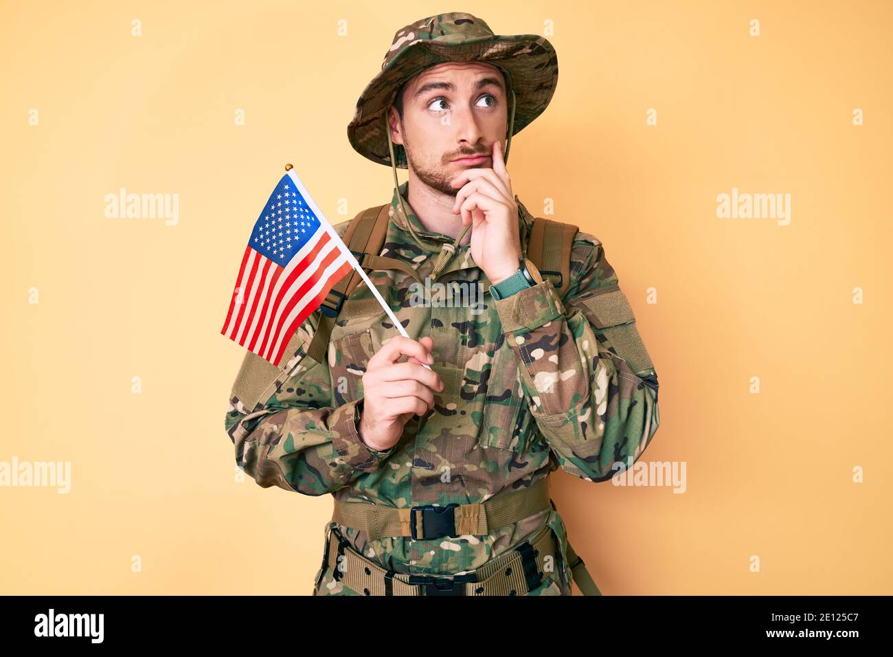 Young caucasian man wearing camouflage army uniform holding usa flag ...