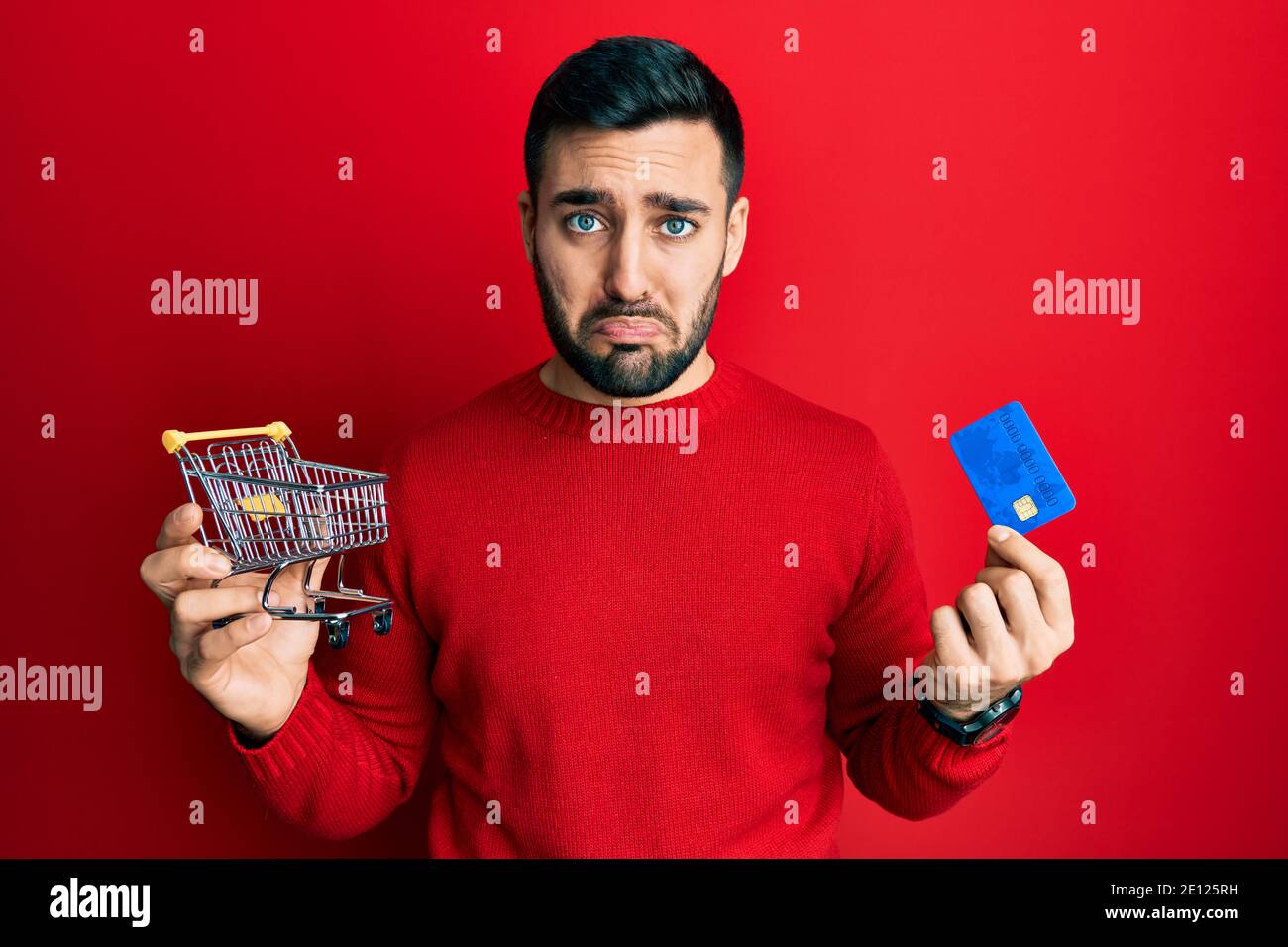 Young hispanic man holding small supermarket shopping cart and credit ...