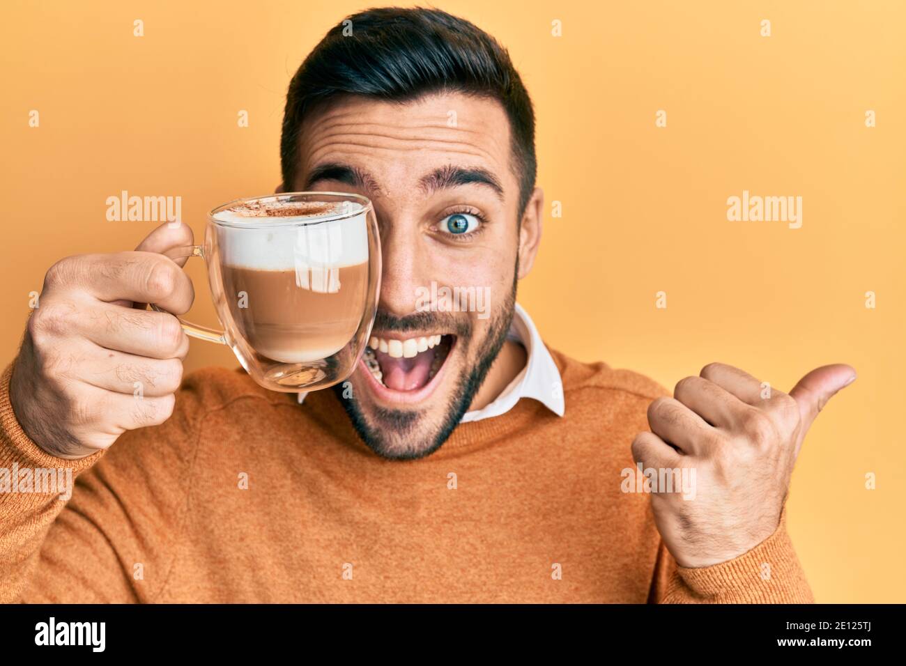 Young hispanic man holding cup of coffee over eye pointing thumb up to ...