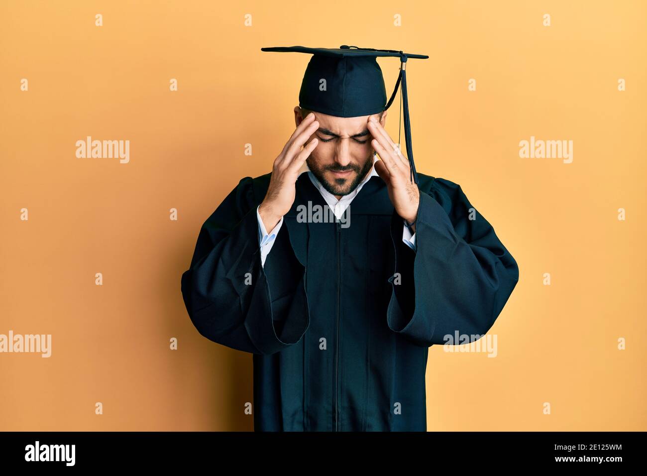 Young hispanic man wearing graduation cap and ceremony robe with hand ...