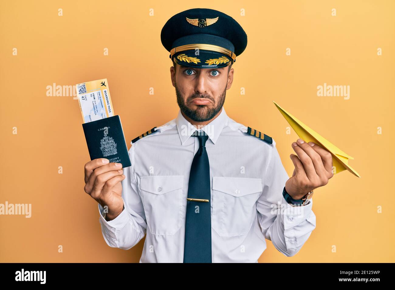 Handsome hispanic pilot man holding paper plane and passport depressed ...