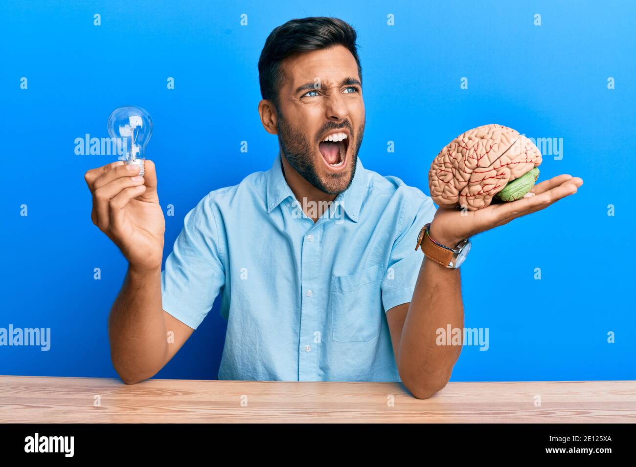Handsome hispanic man holding lightbulb and brain for inspiration and ...