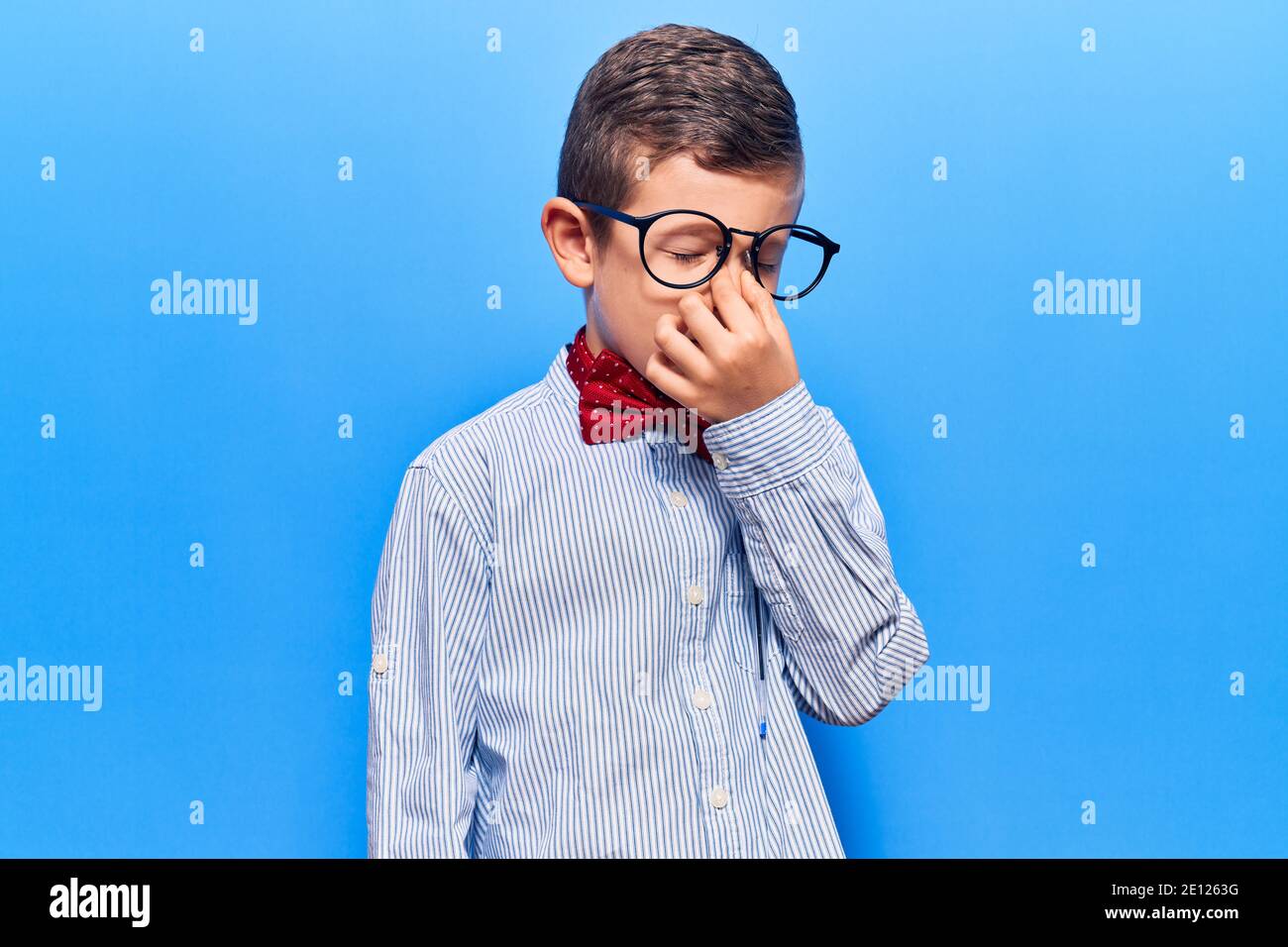 Cute blond kid wearing nerd bow tie and glasses tired rubbing nose and ...