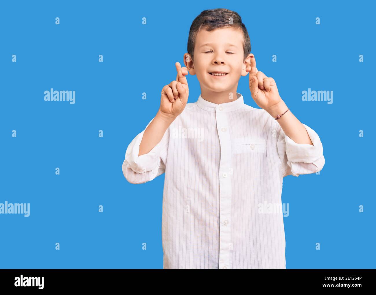 Cute blond kid wearing elegant shirt gesturing finger crossed smiling ...