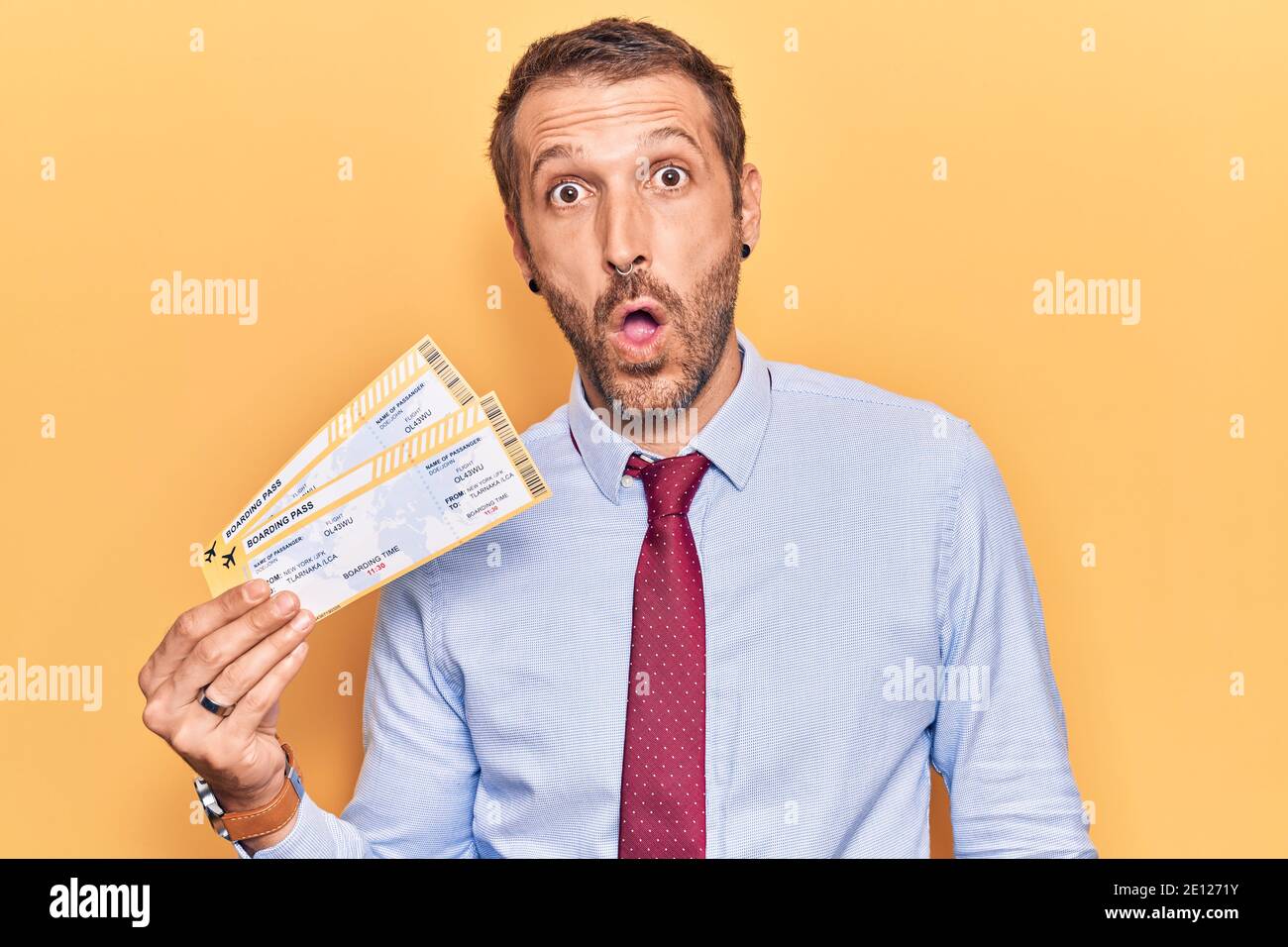 Young handsome man holding boarding pass scared and amazed with open ...
