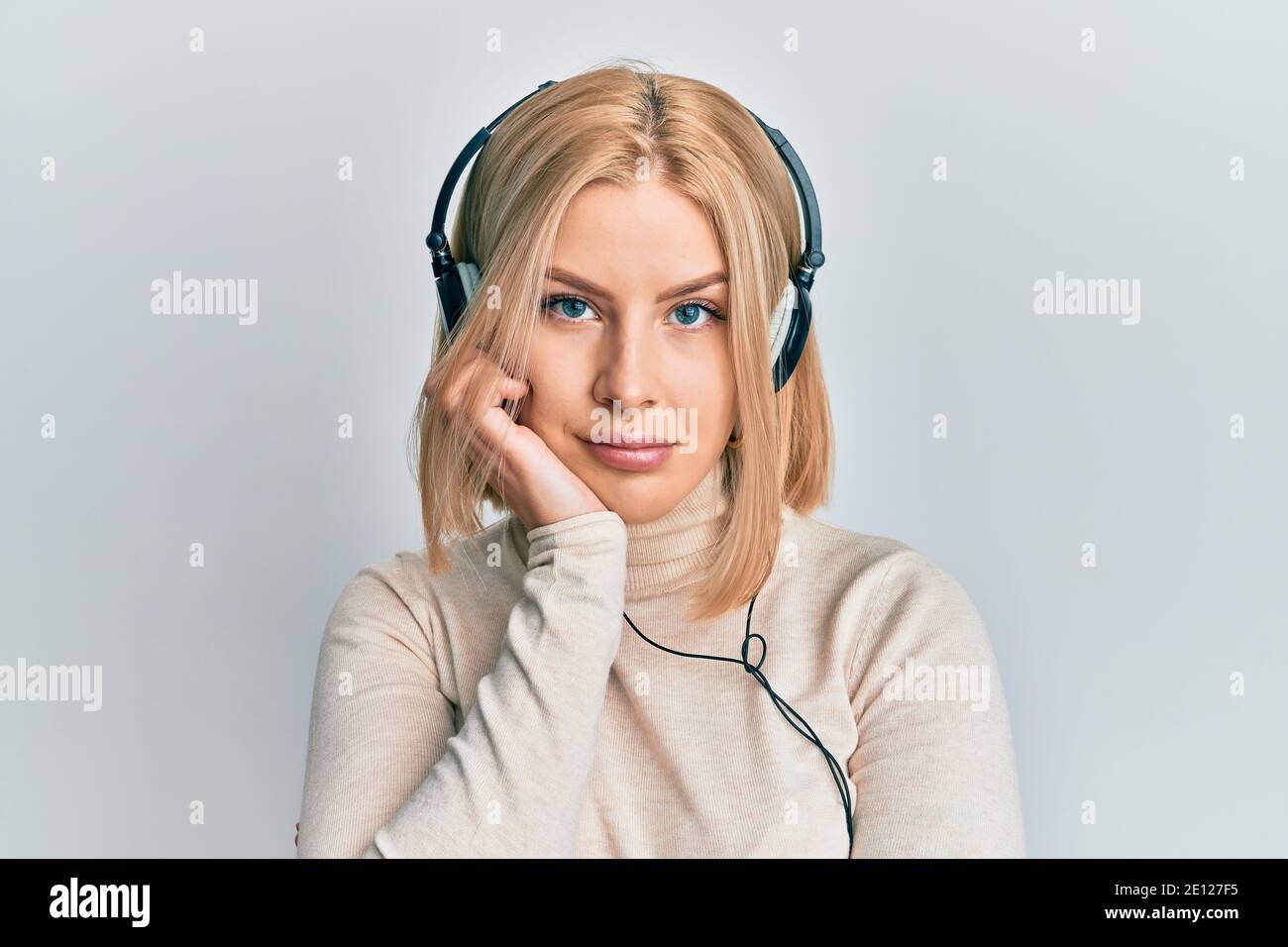 Young blonde woman listening to music using headphones thinking looking ...