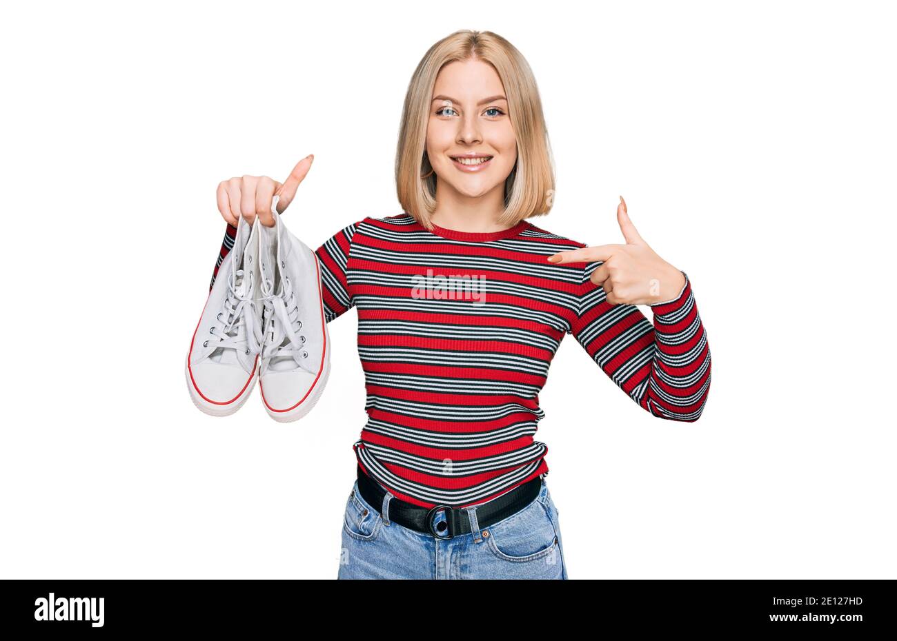 Young blonde woman holding white casual shoes pointing finger to one ...